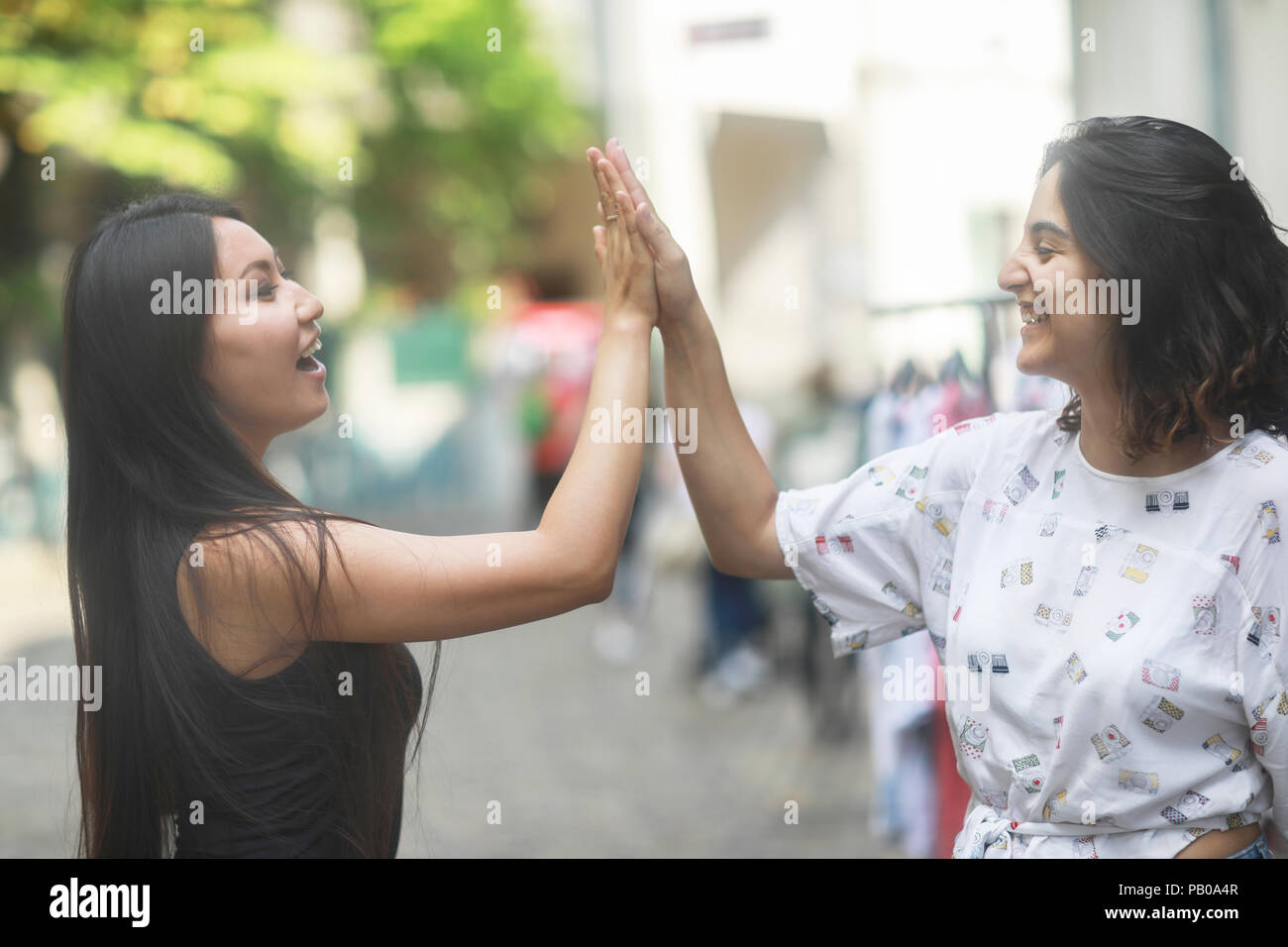 Two women standing in street high fiving Stock Photo - Alamy