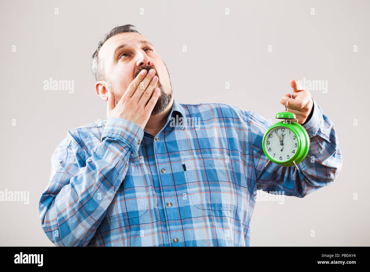 Studio shot portrait of tired man who is holding clock Stock Photo - Alamy