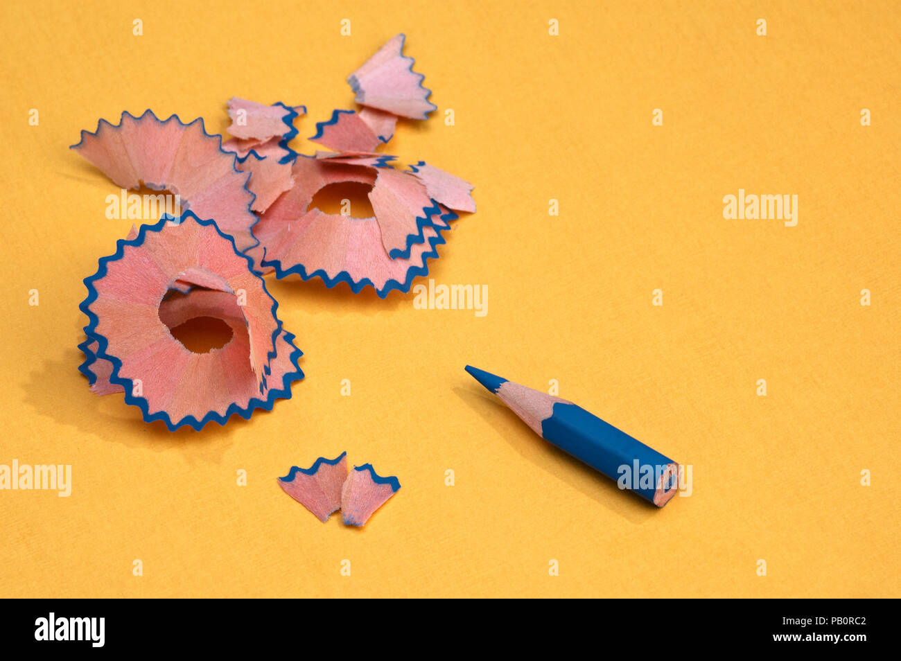 Short blue sharpened pencil with shaving on yellow paper background ...