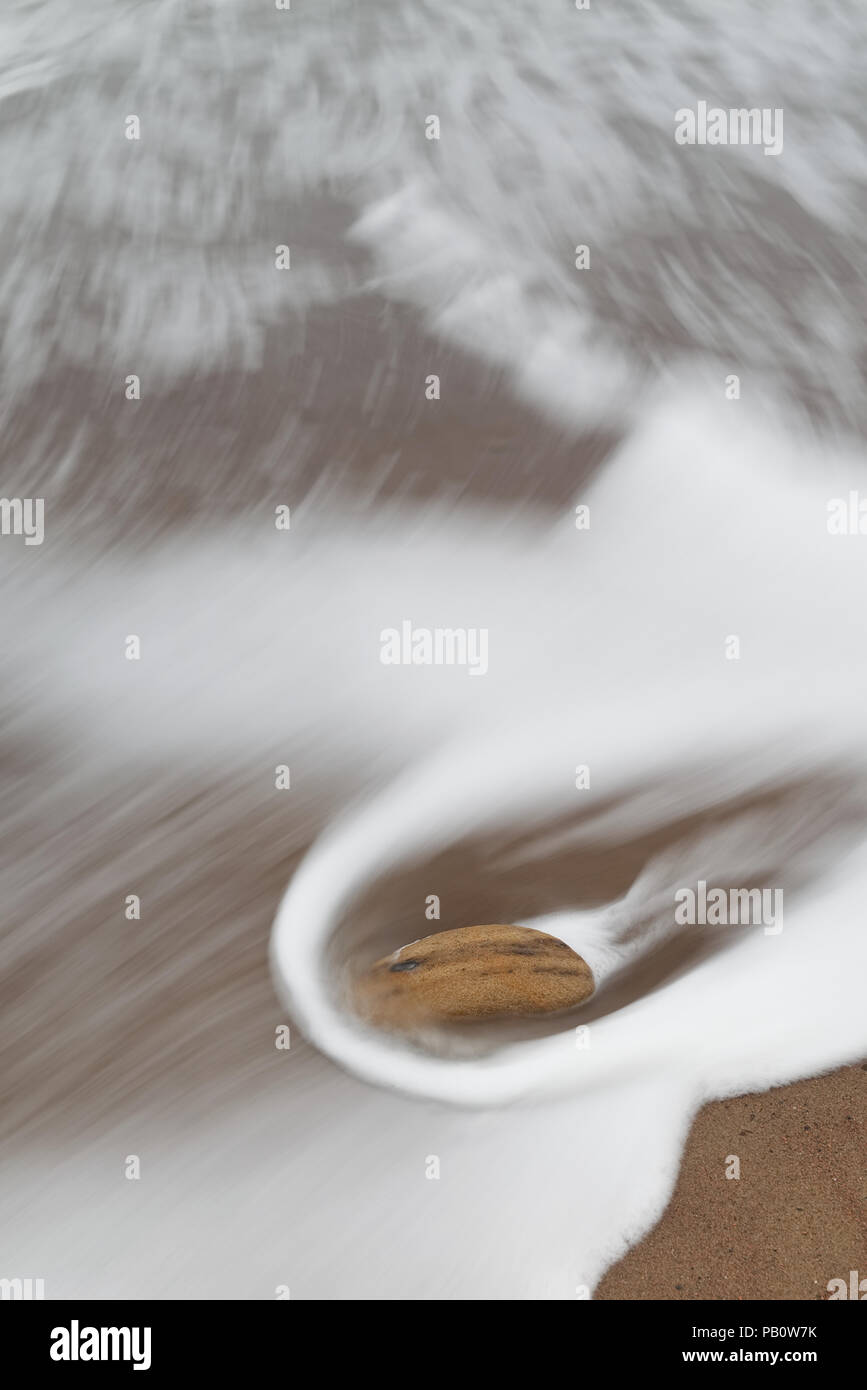 Sandstone rock on sandy beach with silky milky foam waves rolling in ...