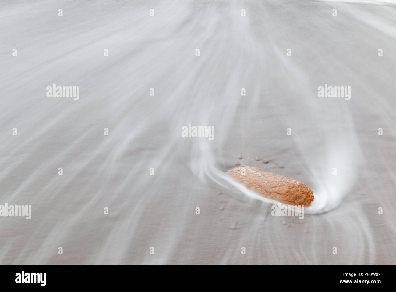 Sandstone rock on sandy beach with silky milky foam waves rolling in ...