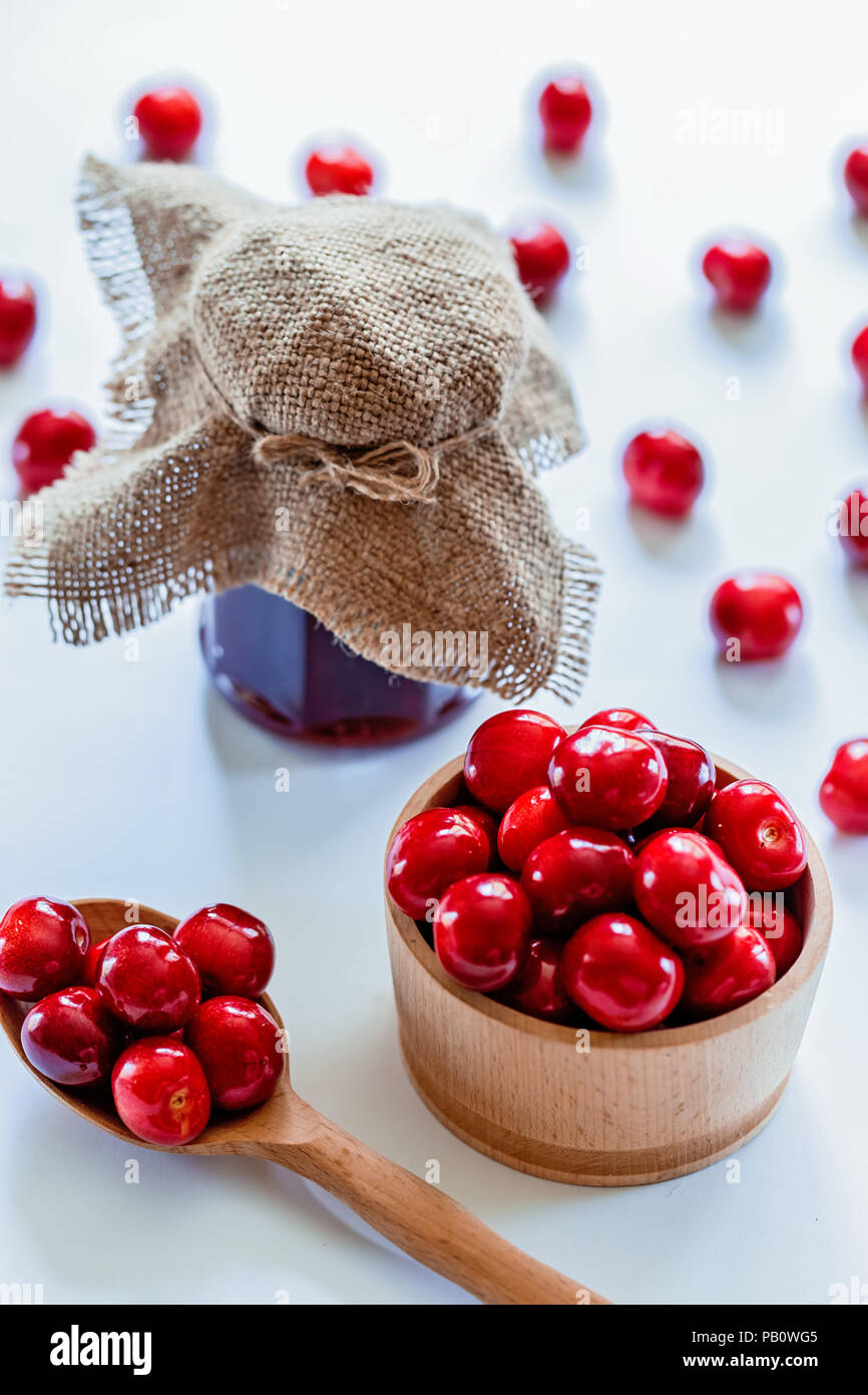 Red ripe cherries with jam jar and wooden spoon on white background ...