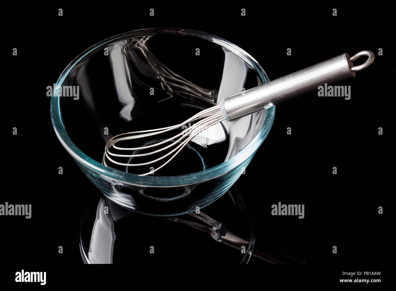 Glass transparent bowl with metal whisker inside on black background ...