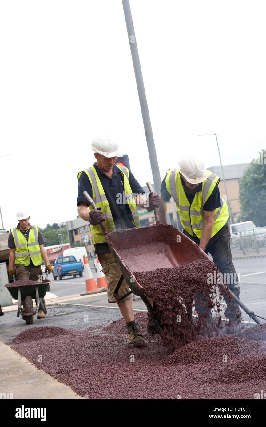 Workmen pouring ashphaltfrom a wheelbarrow and Laying red asphalt on to ...