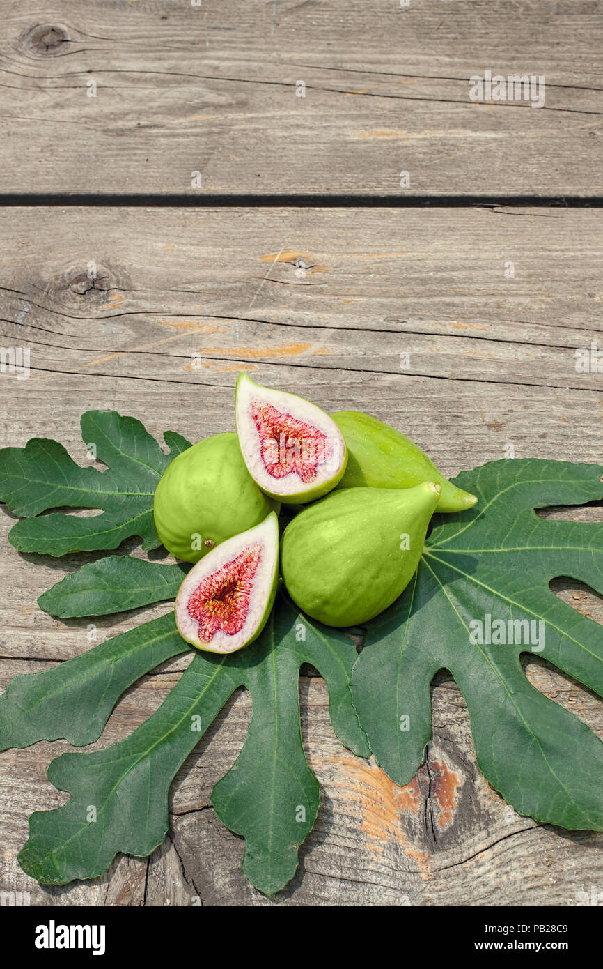 halved fig on figs and fig leafs, vertical, wood board as background ...