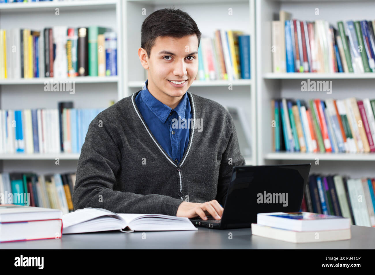 Happy student is learning in library. He is using laptop Stock Photo ...