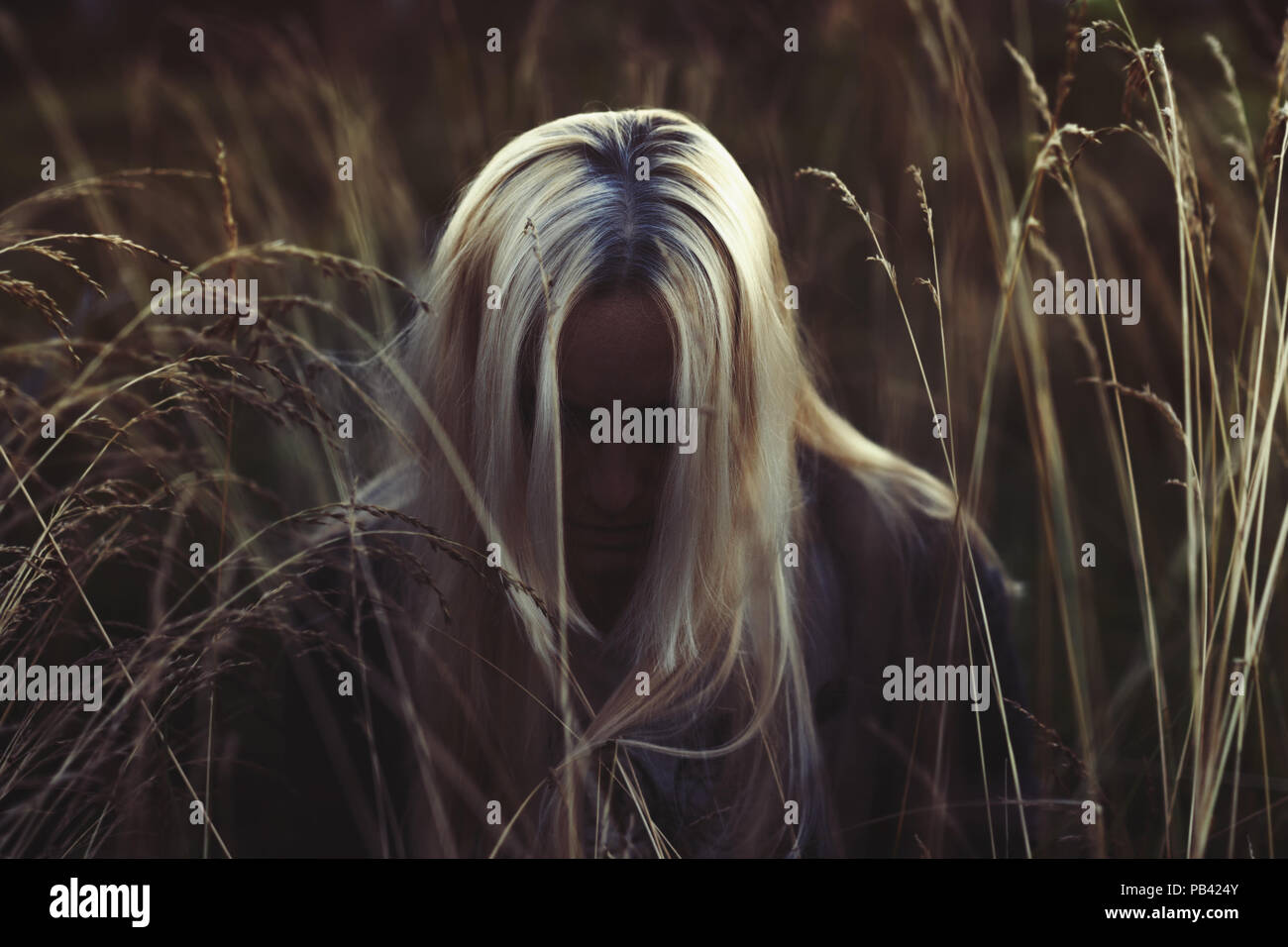 Woman with long blonde hair bowing her head in tall grass field in the ...