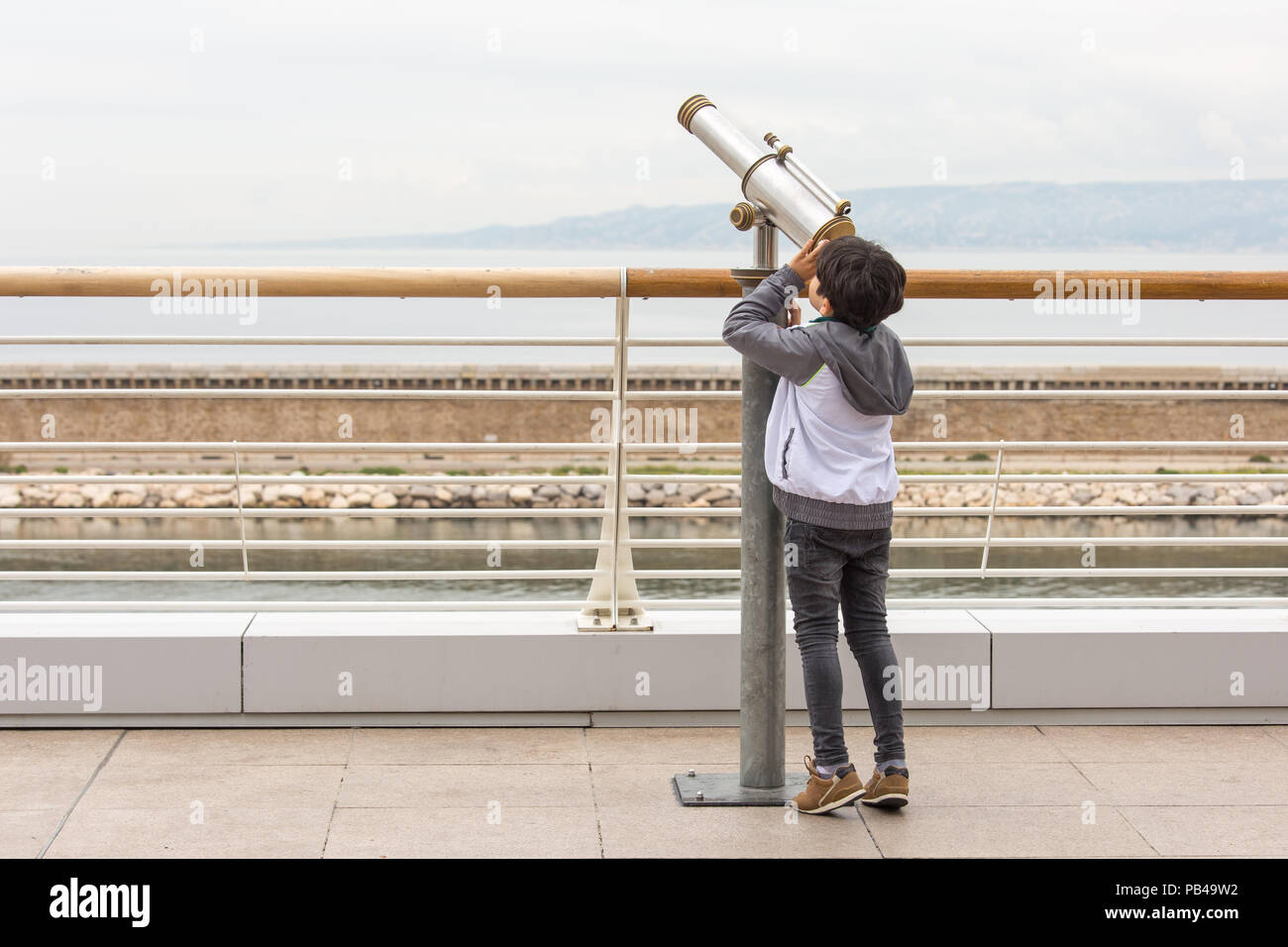 A young boy standing on his toes, exploring the sky with a telescope ...