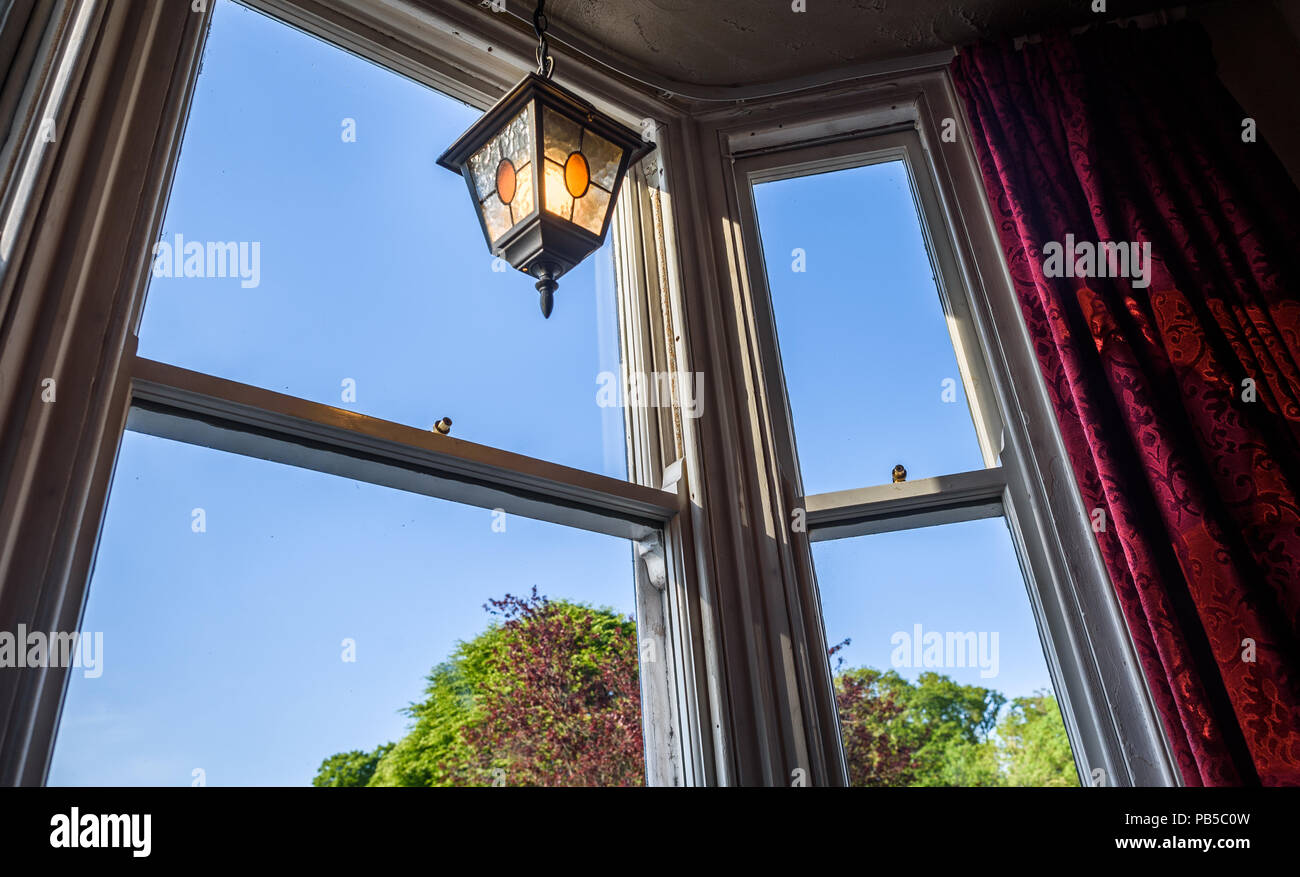 A traditional British pub window with old fashioned lamp and red velvet ...