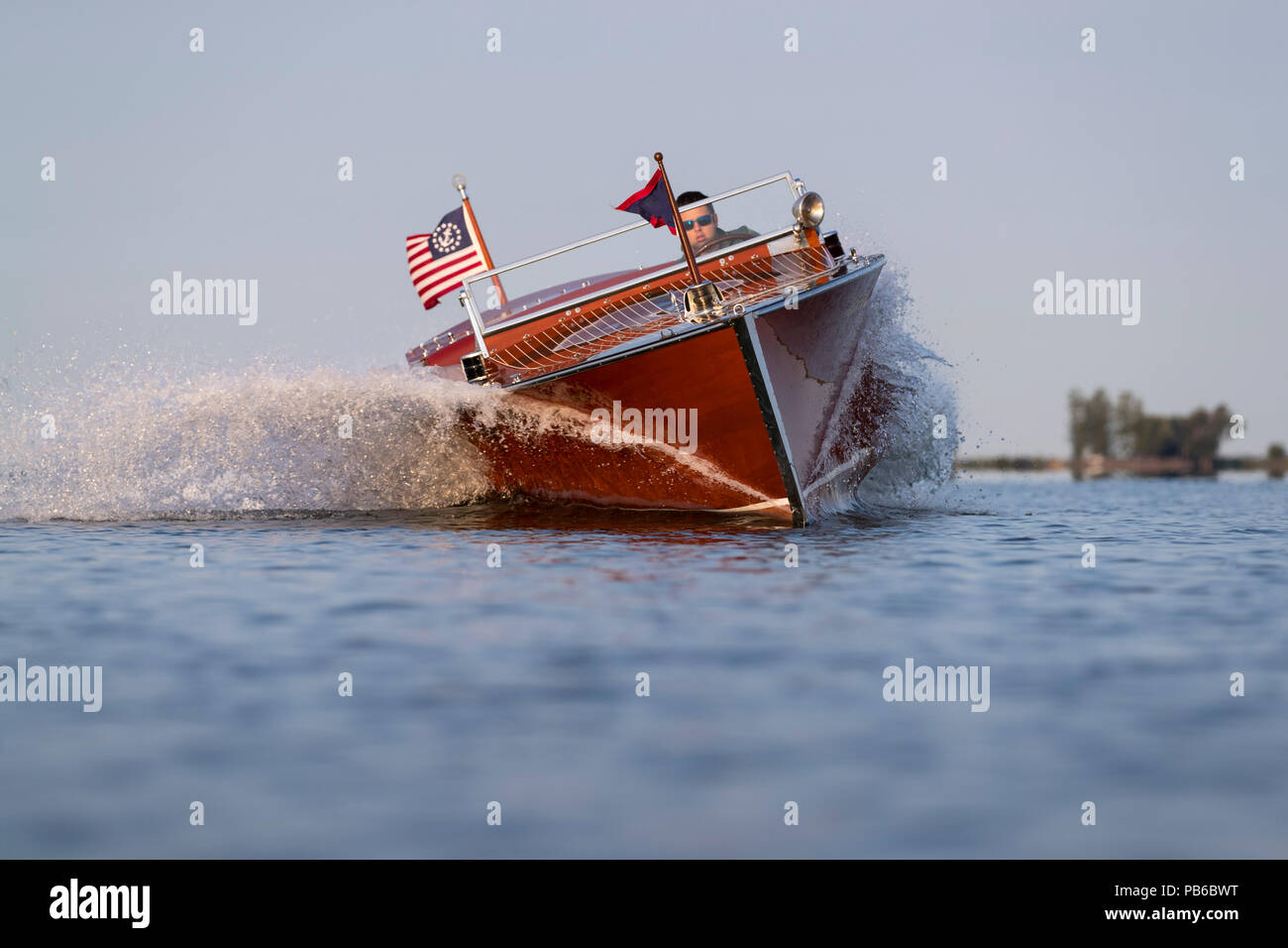 A man driving an antique, wooden speedboat and turning sharply Stock ...