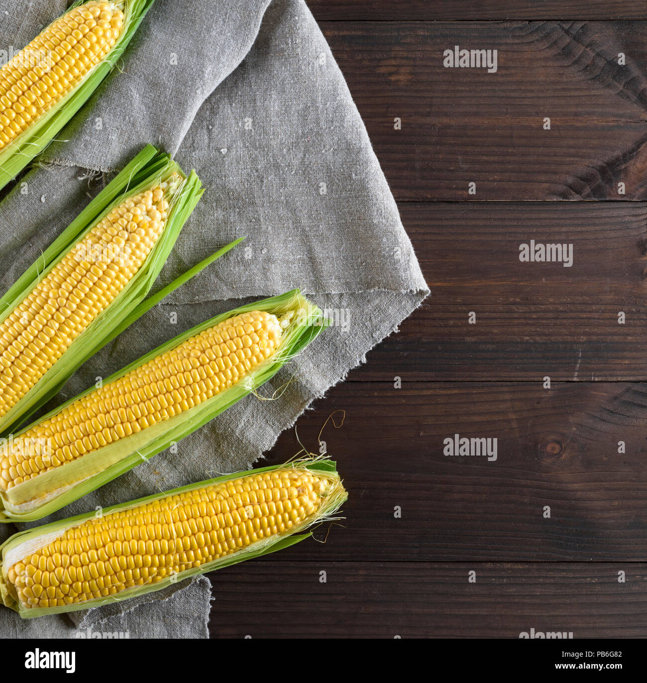fresh ripe corn cobs on a gray linen napkin, wooden background, empty ...