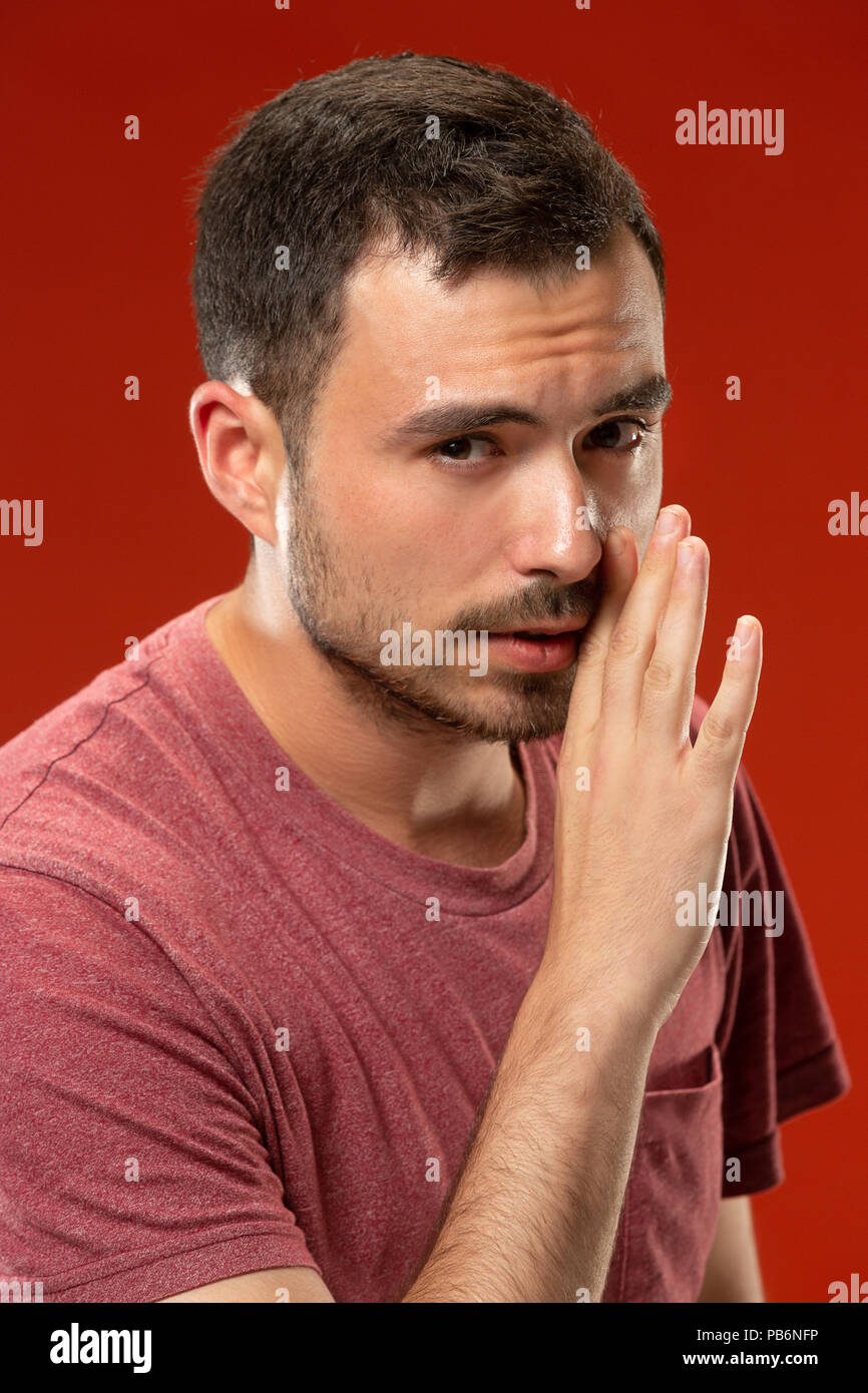 The young man whispering a secret behind her hand over red background ...