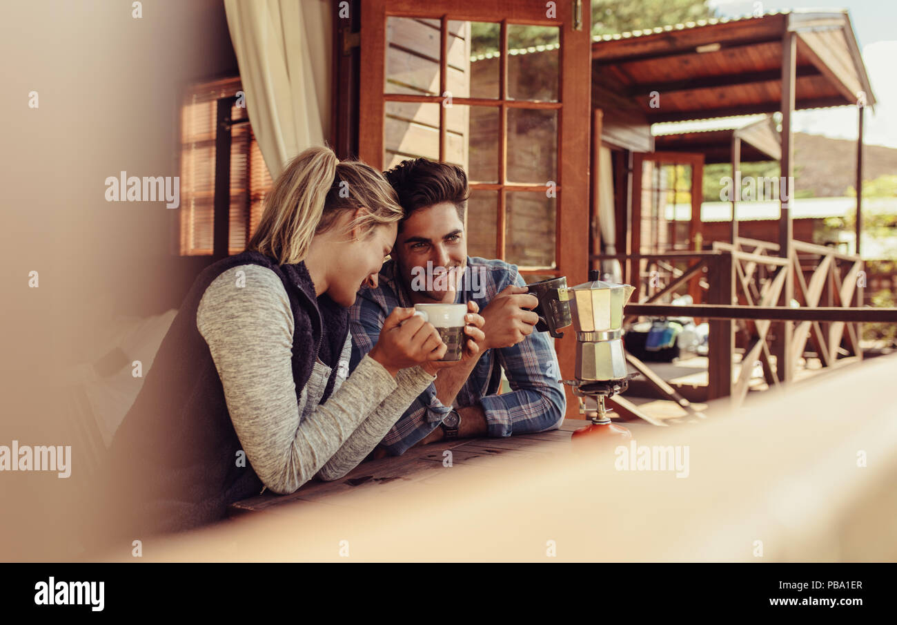 Loving Young Couple Sitting Outside A Wooden Cabin Having Coffee And