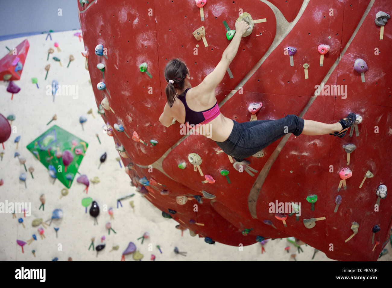 Photo from back of athlete woman on red climbing ball in sports hall ...
