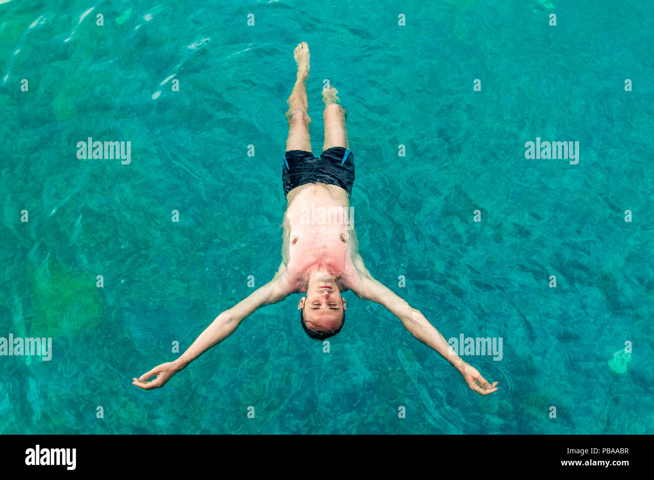 Top view of a young man floating in a swimming pool with open arms ...