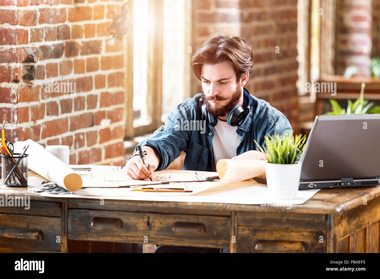 Concentrated young architect working with blueprint while sitting with ...