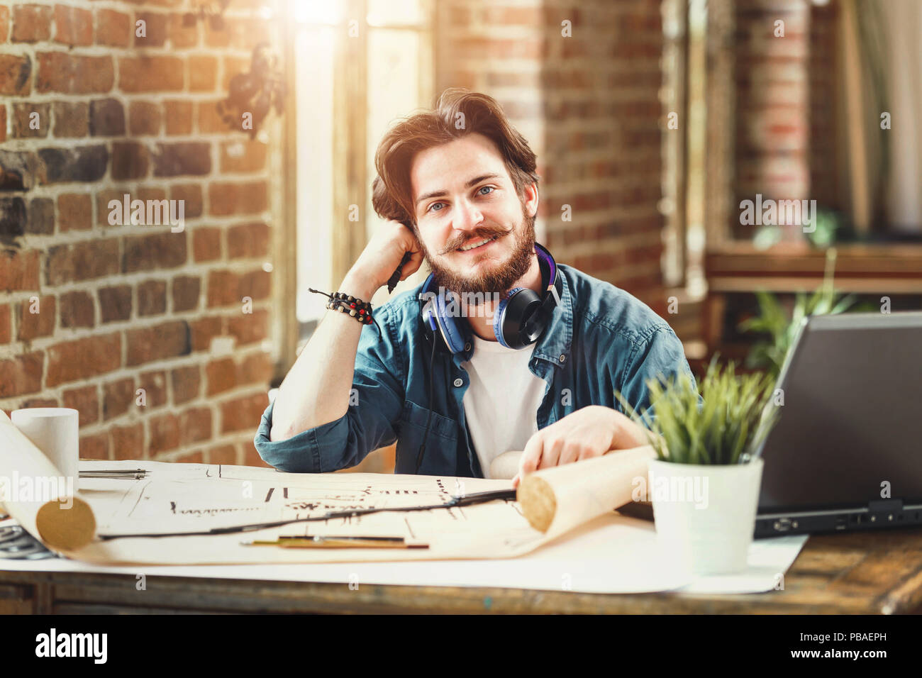 Male bearded architect smiling to the camera sitting at his desk at the ...