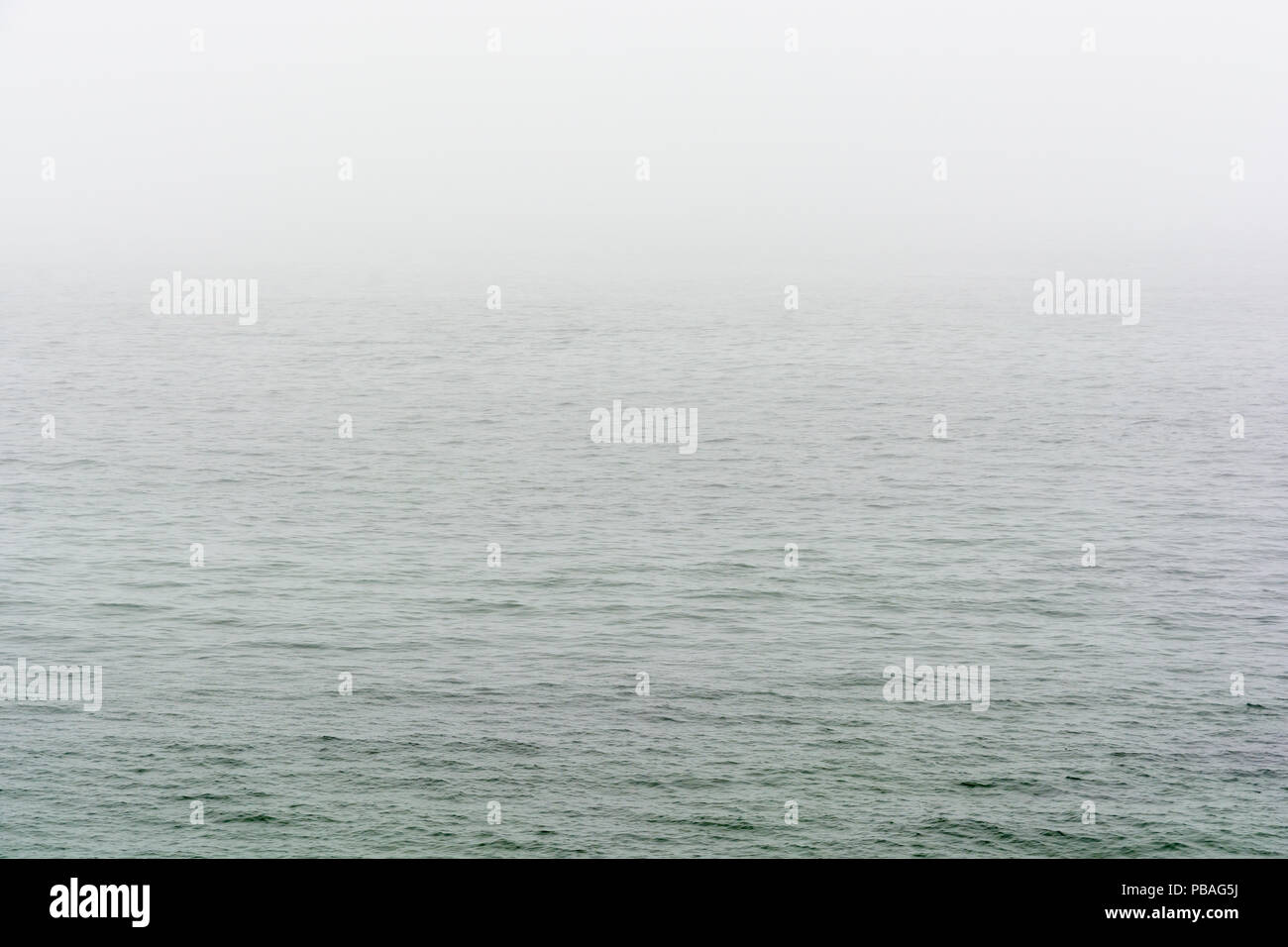 Flat grey sea with wavelets disappearing in the fog Stock Photo - Alamy
