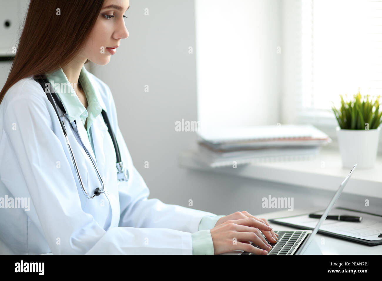 Young female doctor typing on laptop computer while sitting at the ...