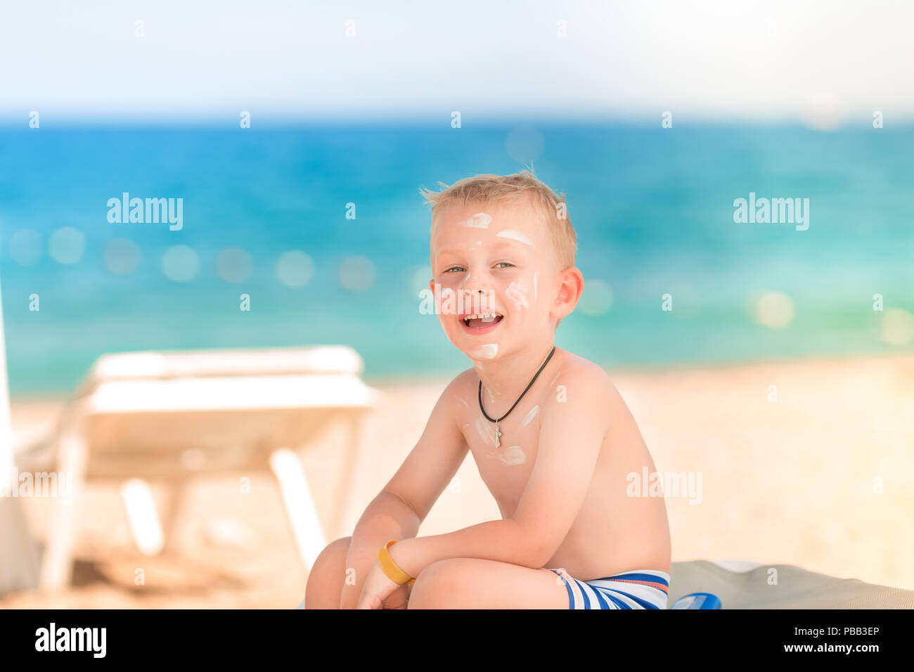 Cute little boy with sunscreen on holding the bottle of sunscreen ...