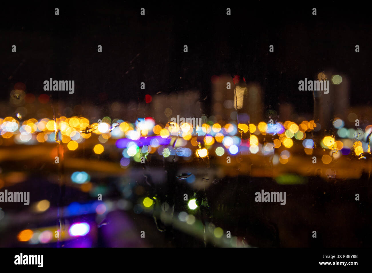 Drops of night rain on window, on back plan washed away lights of the ...
