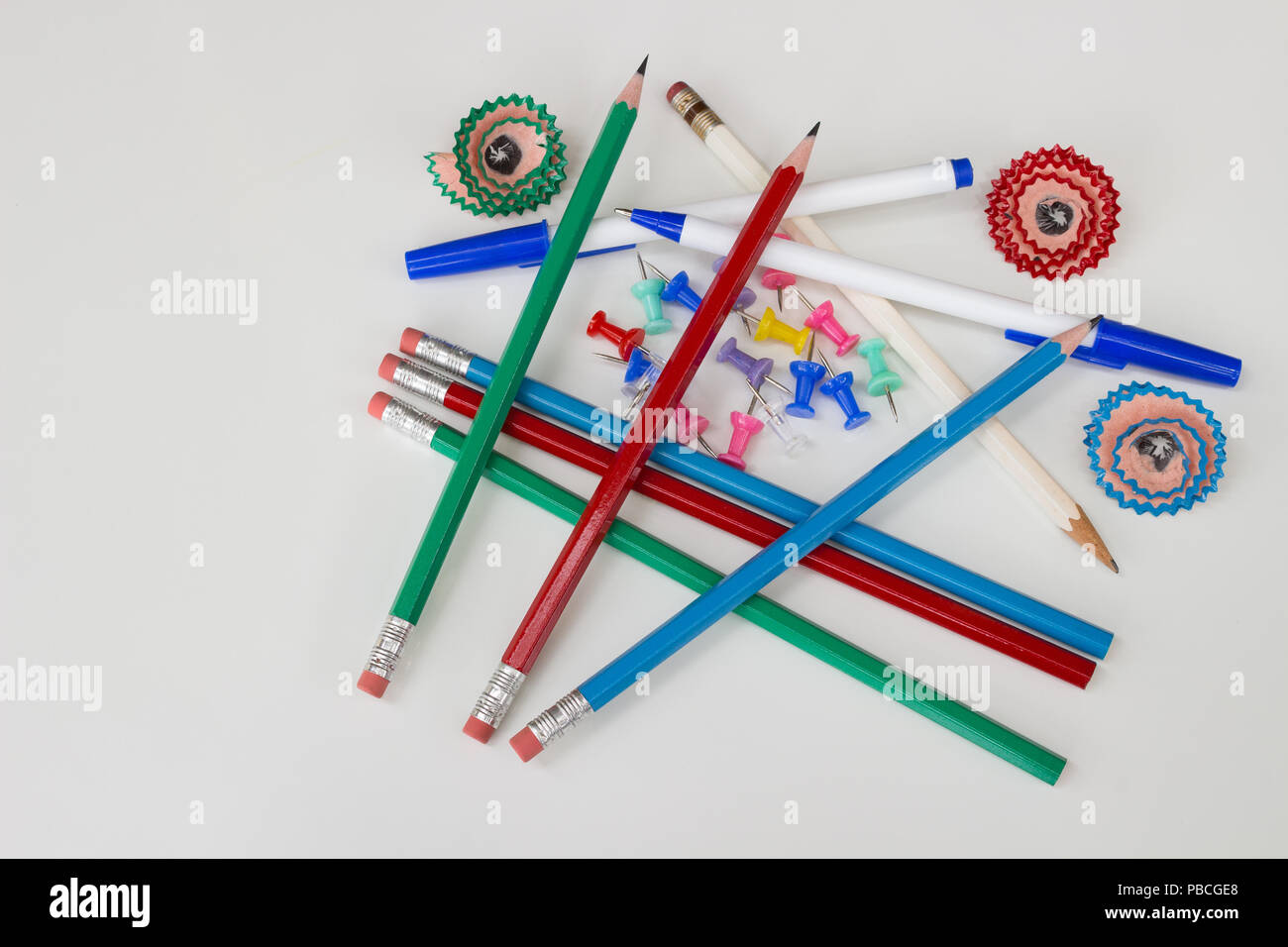 Pens, pencils, push pins, and flower pencil shavings on white ...