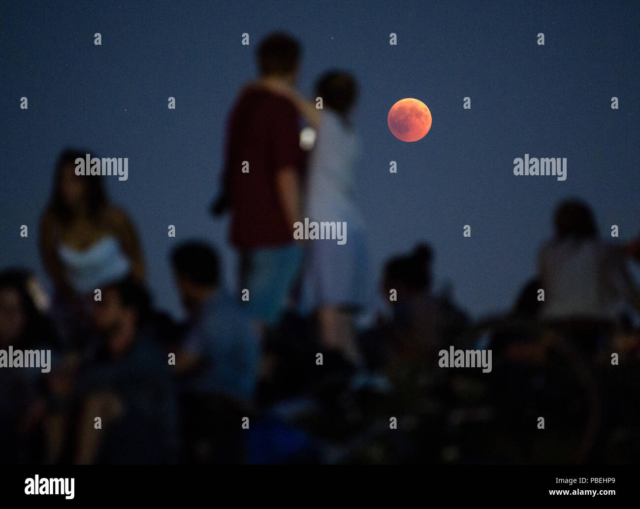 Munich, Germany. 27th July, 2018. Numerous people observe the lunar eclipse with the reddish ...