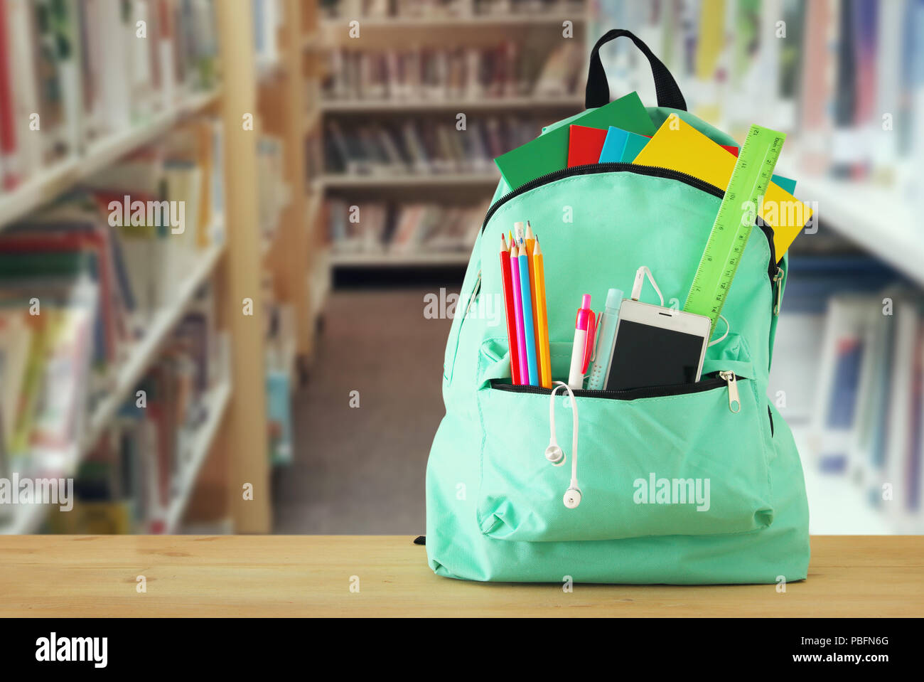 school bag with stationery and notebooks in front of shelves with books ...