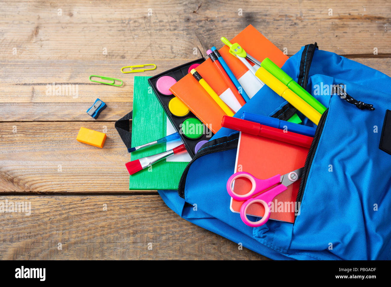 Back to school concept. Blue backpack full of school supplies on wooden ...
