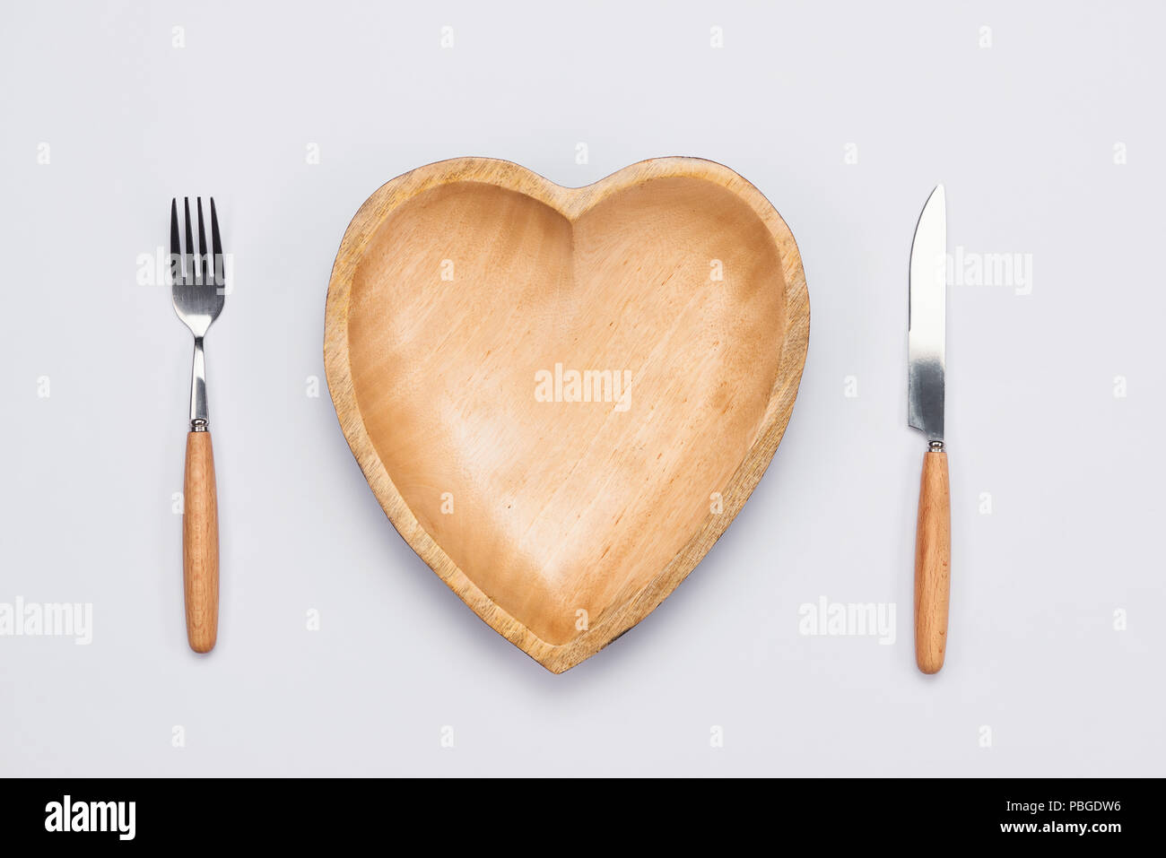 Wooden plate in shape of heart, table knife and fork on white ...
