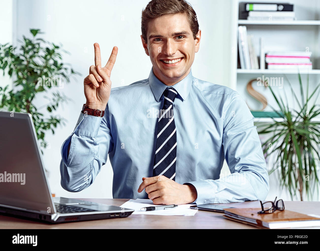Successful businessman showing victory sign. Photo of young man working ...