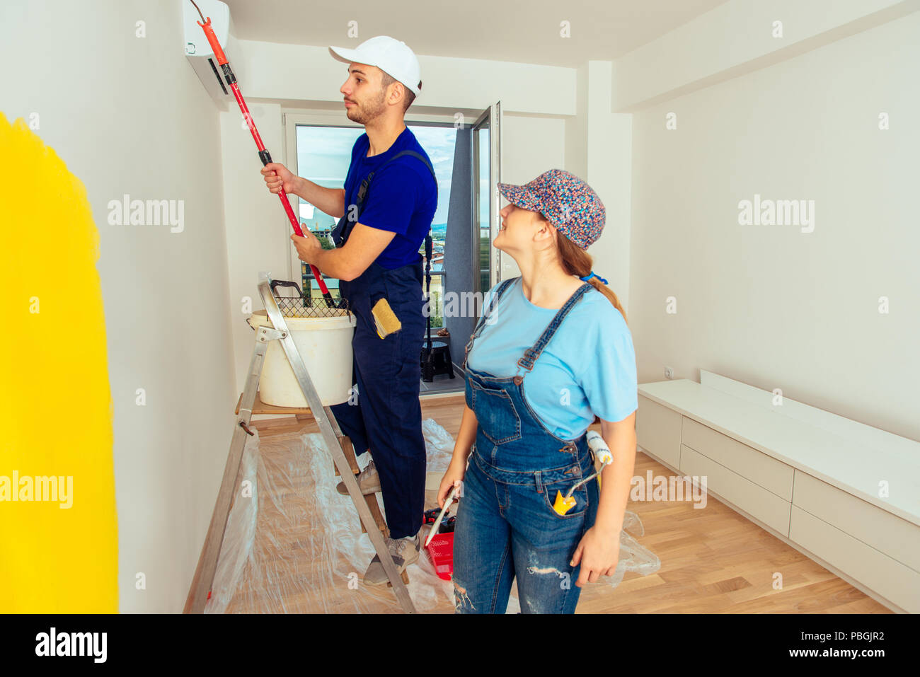 Man decorator coloring wall with yellow color while standing on ladder ...