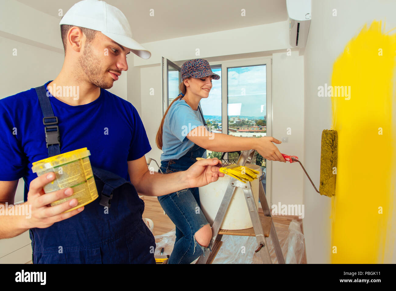 Adorable couple painting living room with paint stick roller and ...