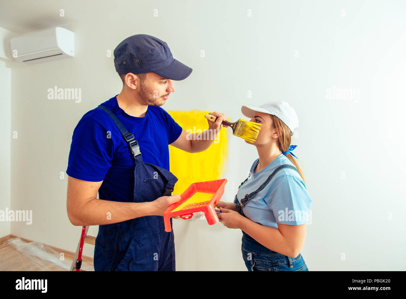 Young couple having fun while painting wall at home in yellow with ...