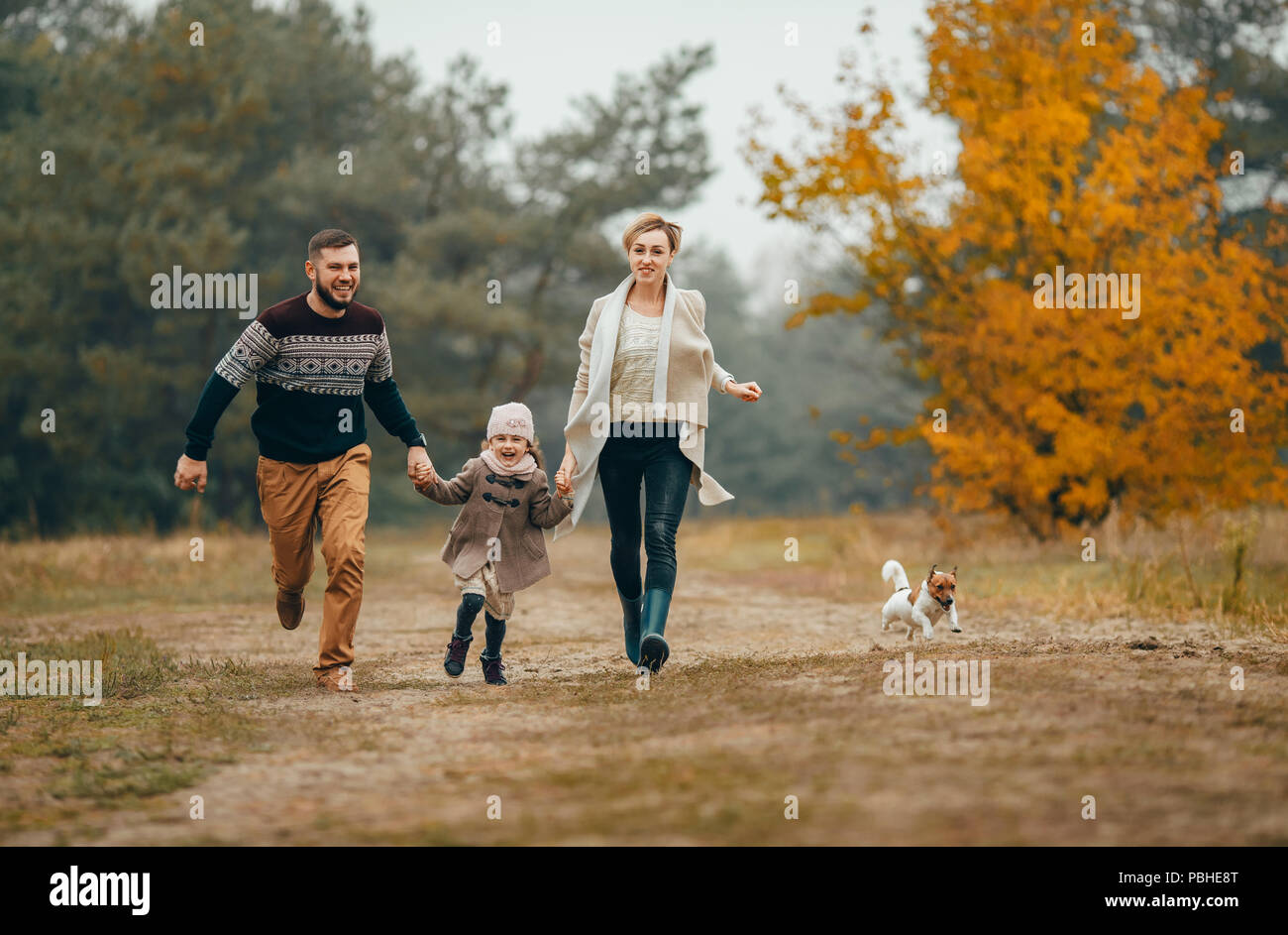 Happy parents with their daughter hold hands and run at forest path ...