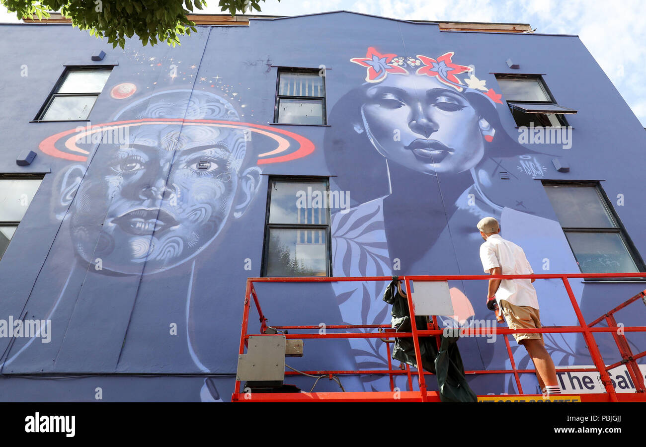 An artist looks up at his mural on the side of the Salvation Army ...