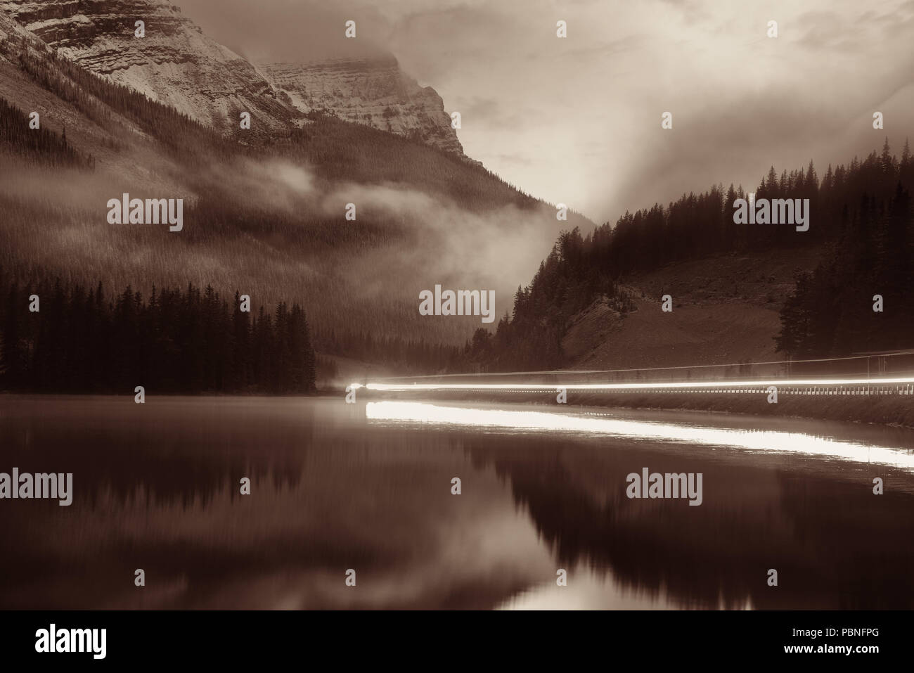 Mountain lake and traffic light trail with reflection and fog at sunset ...