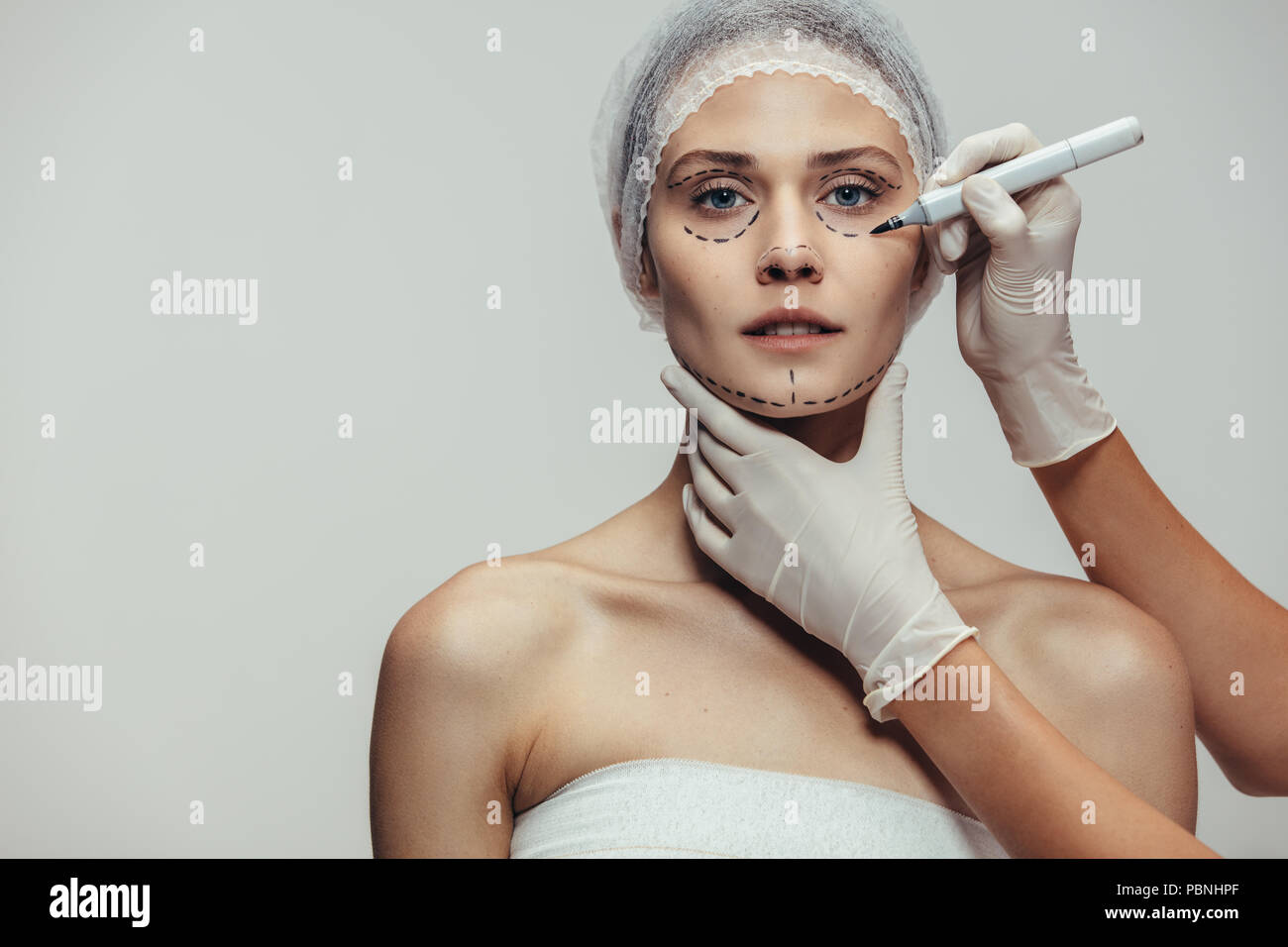 Beautician drawing dotted lines on female face before plastic surgery ...