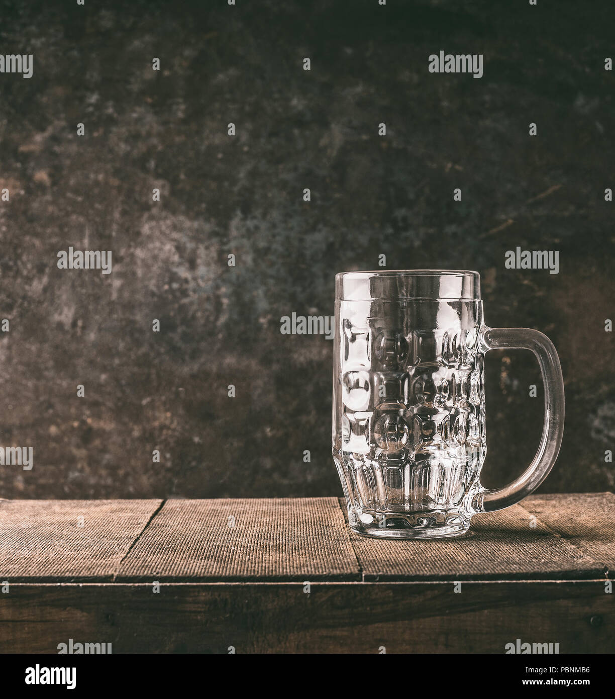 Empty mug of beer on a rustic table opposite a dark wall, front view ...