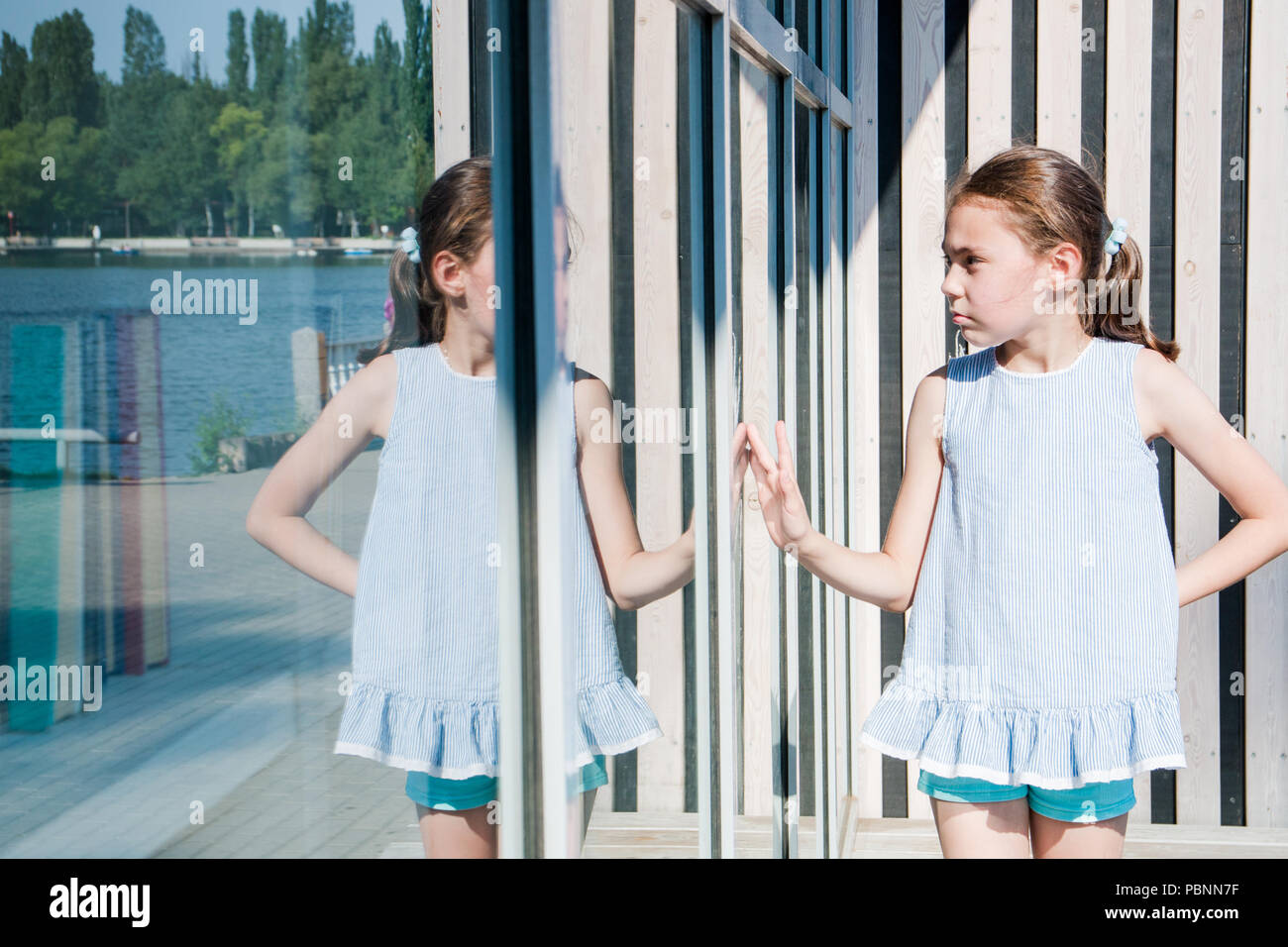 small cute girl looks at her reflection sunny day Stock Photo - Alamy