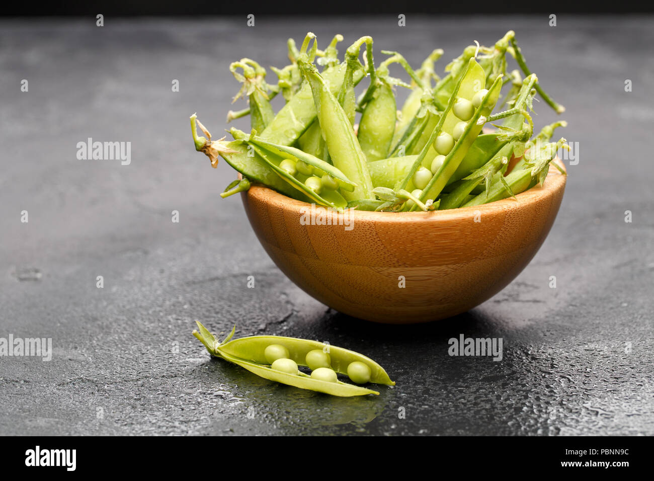 Photo of green pea pods in wooden plate on blank black table with pod ...