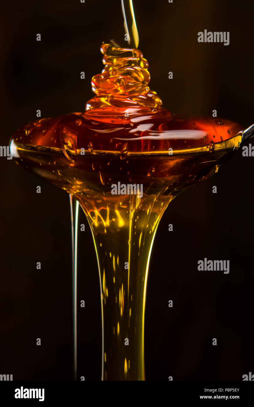 Honey Pours from Overflowing Spoon in front of dark background Stock ...