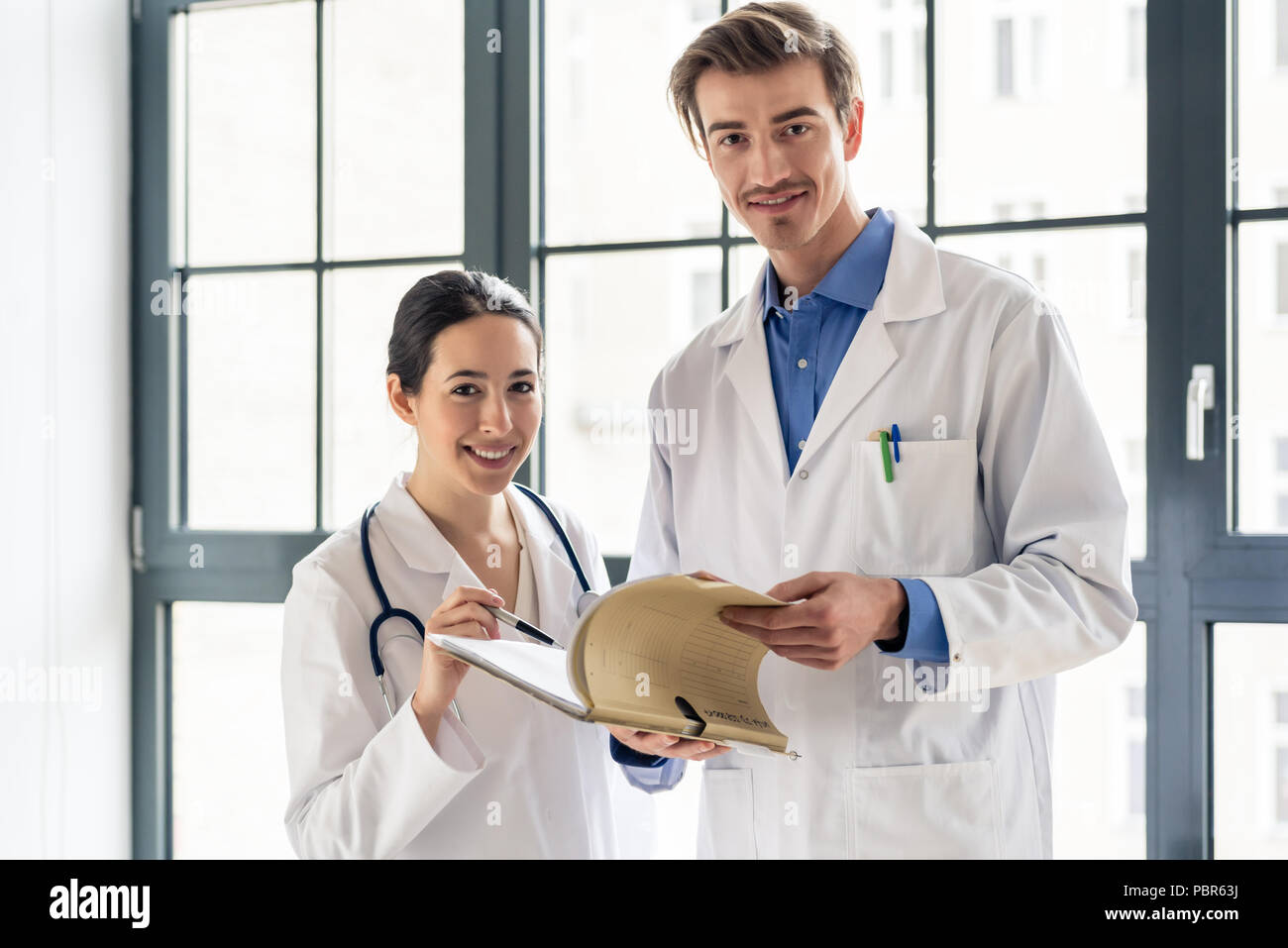 Two dedicated doctors smiling while holding a folder with medical ...