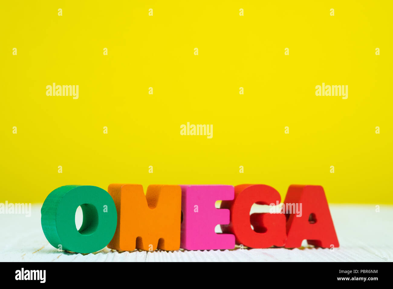 OMEGA text alphabet on white wooden table. yellow wall background with ...