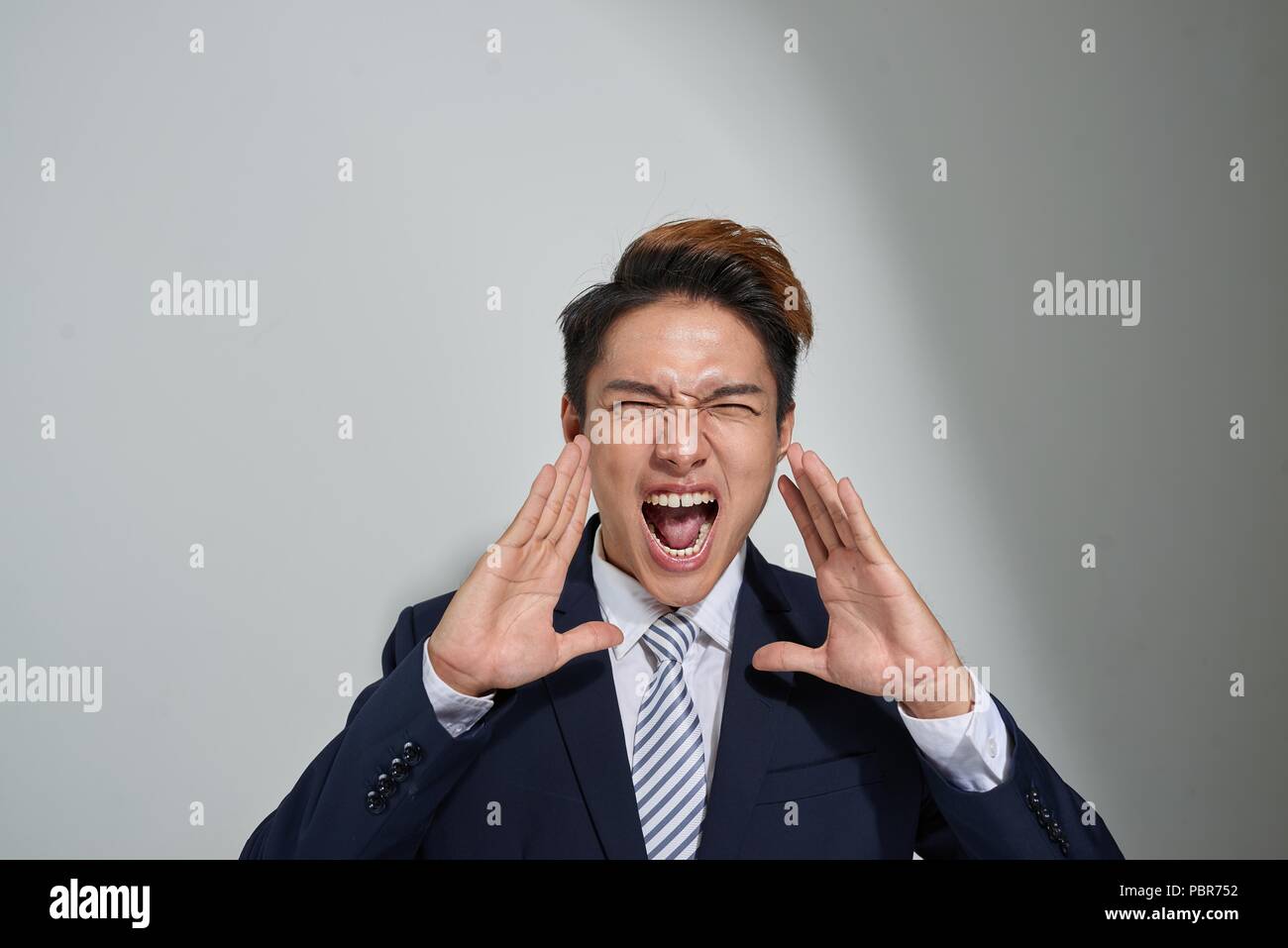 young Asian business man shouting with hands cupped to his mouth ...