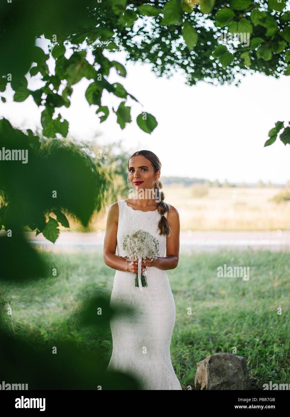 Bride standing near a tree with her bridal bouquet Stock Photo - Alamy