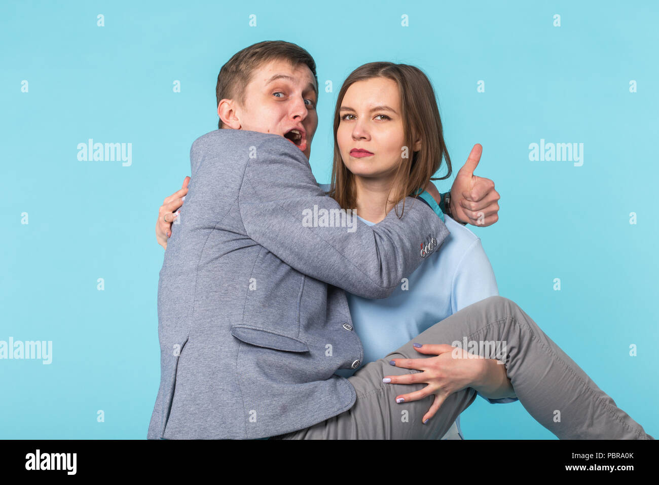 Joking funny couple - girl keeping her boyfriend on her hands over blue ...