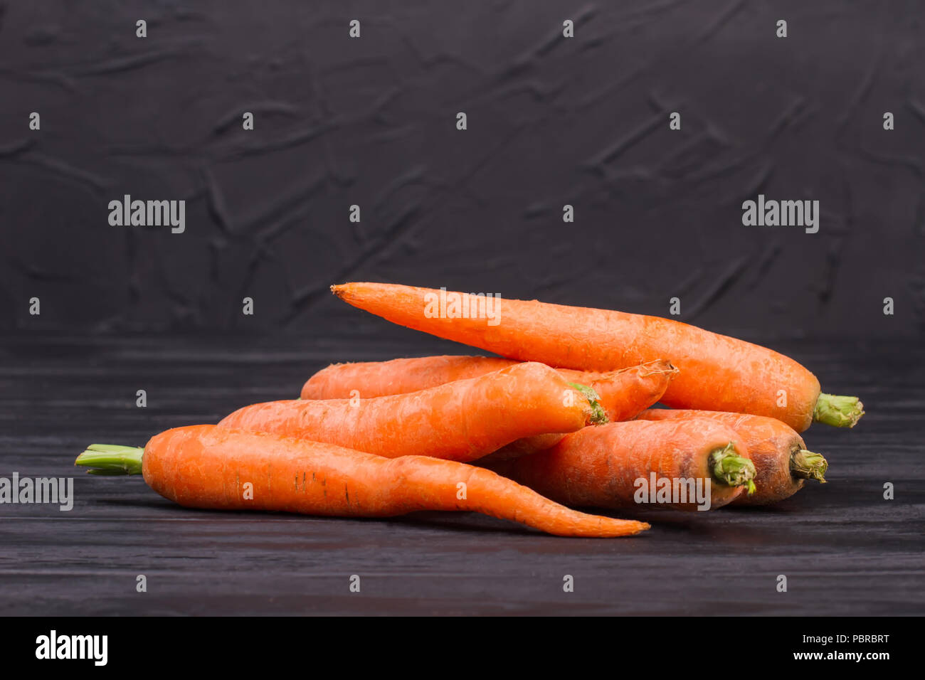 Heap of ripe raw carrots on black background. Close up. Dark wooden ...