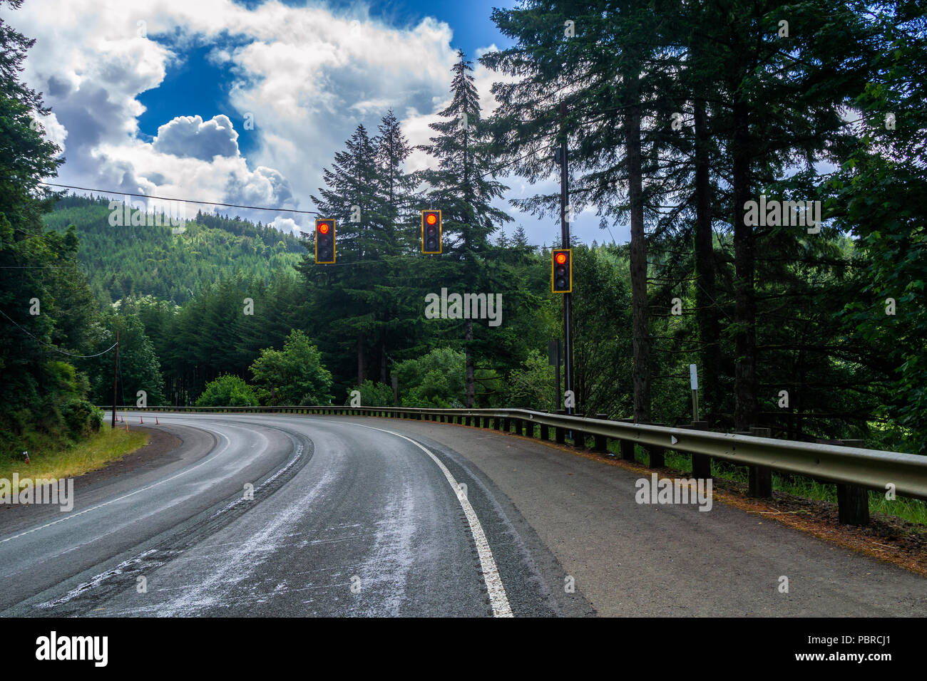Three red traffic lights hanging above the road through a mountain ...