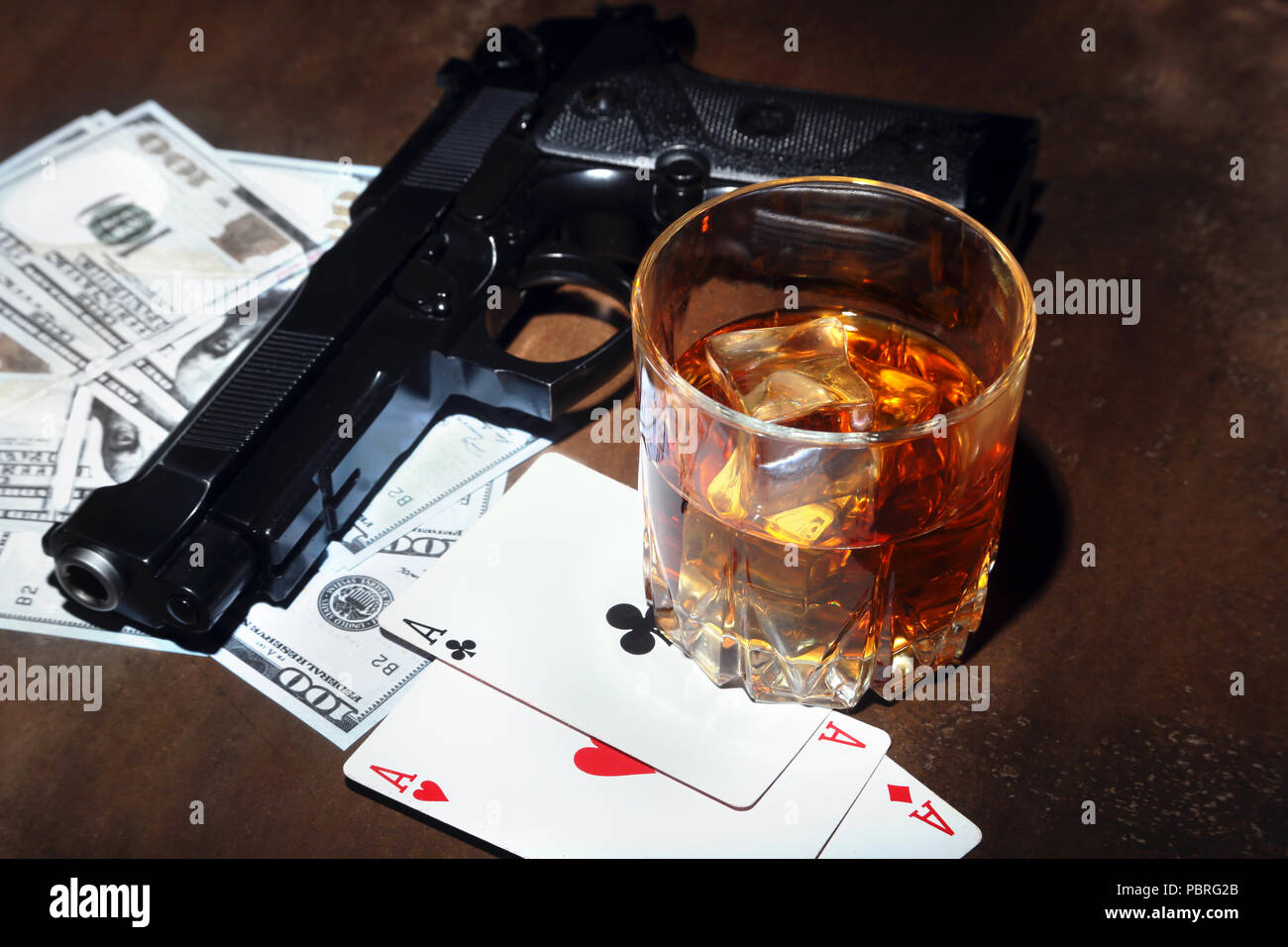 Glass of whiskey or cognac, gun, playing cards with money on the black ...